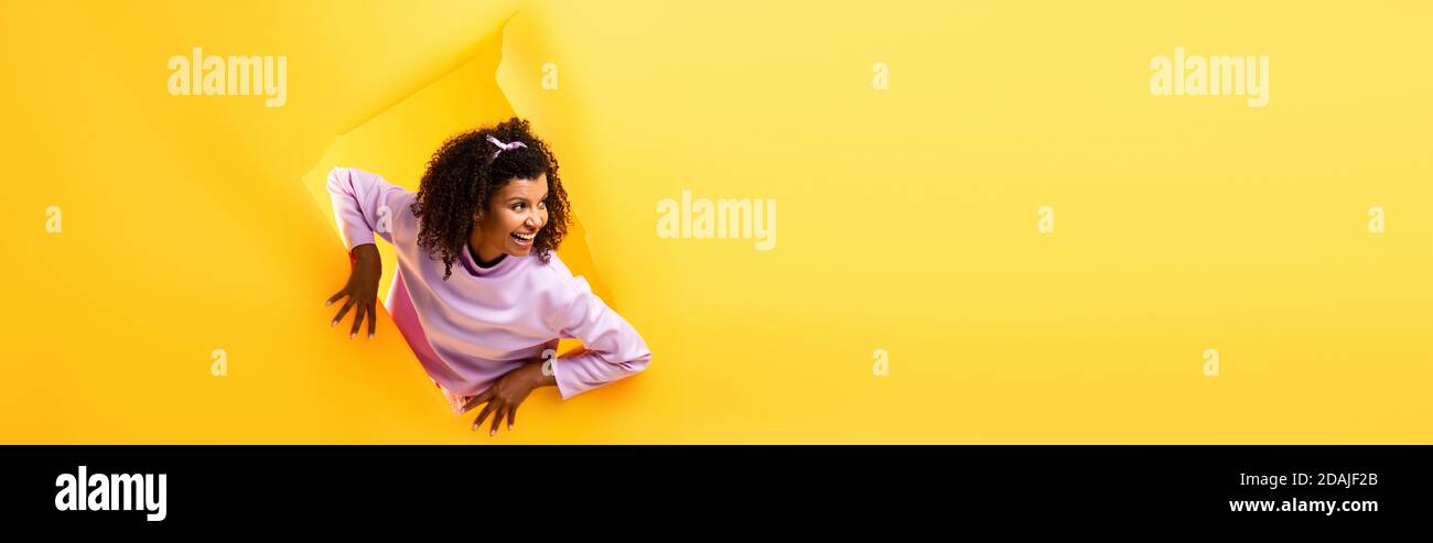 curious african american woman looking away through hole in ripped ...