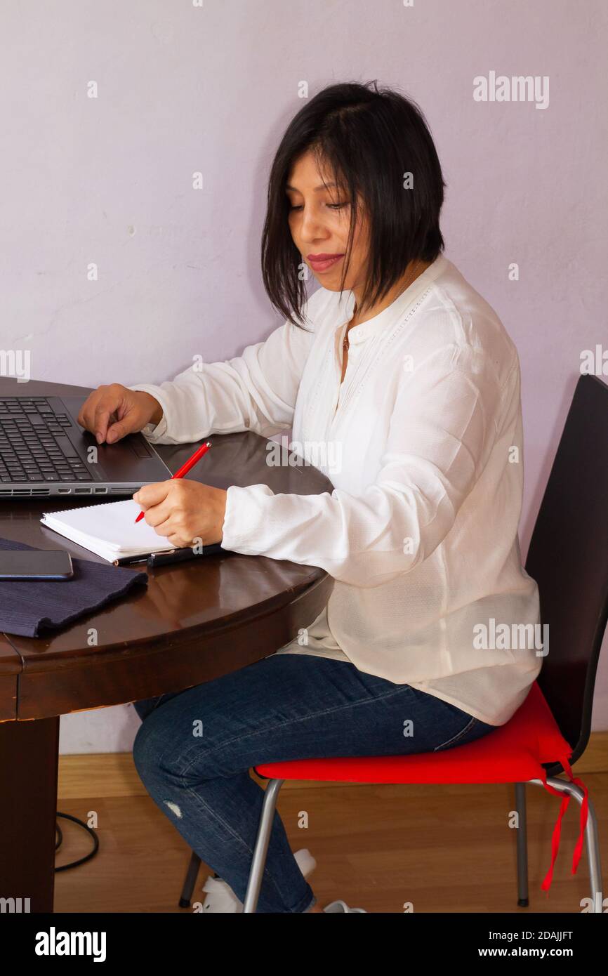 Latina woman taking notes in her notebook next to her computer dressed ...
