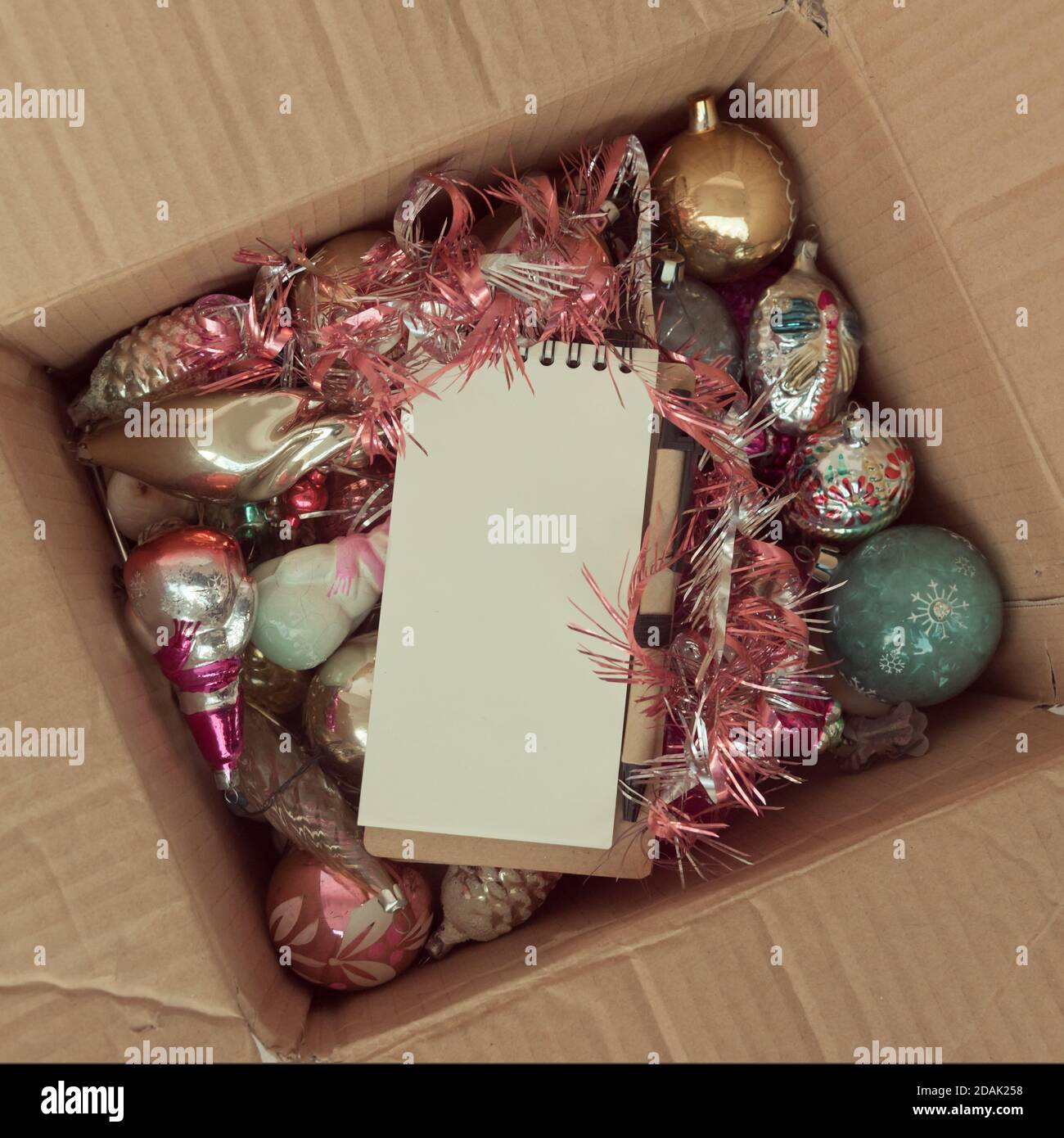 An open cardboard box with old glass Christmas decorations. On top of a ...
