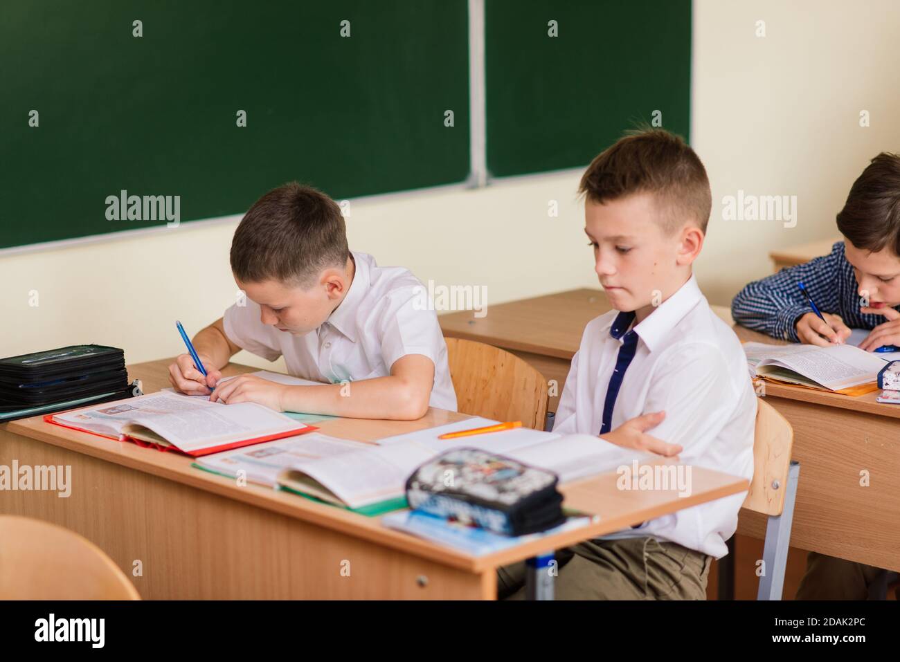 Elementary schoolchildren writing in books in classroom Stock Photo - Alamy