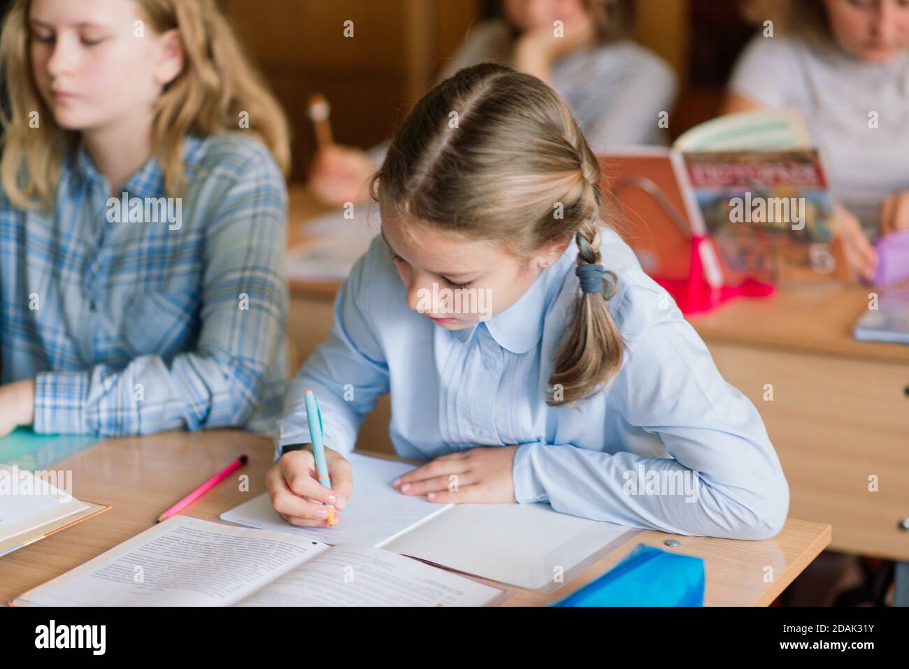 Elementary schoolchildren writing in books in classroom Stock Photo - Alamy