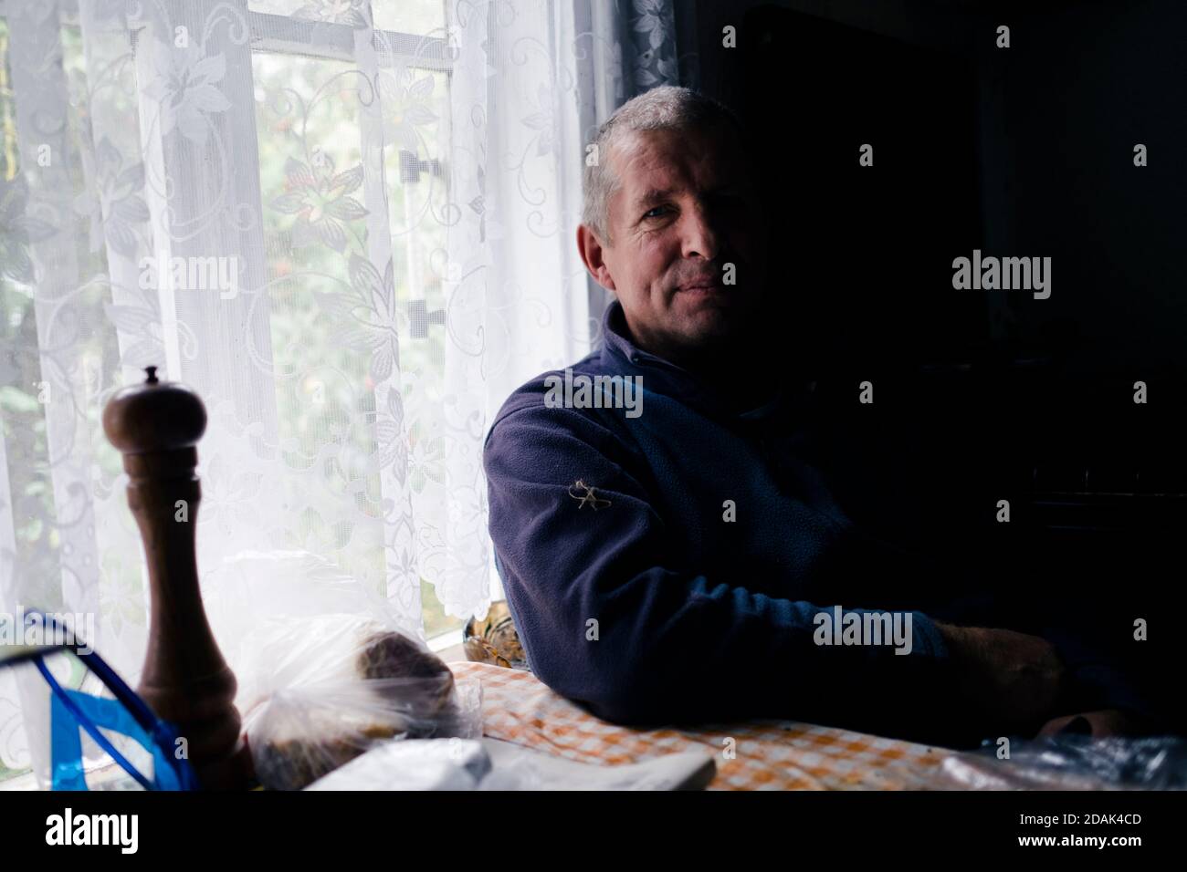 A man sitting by the window; shadow falls on half of his body and face ...
