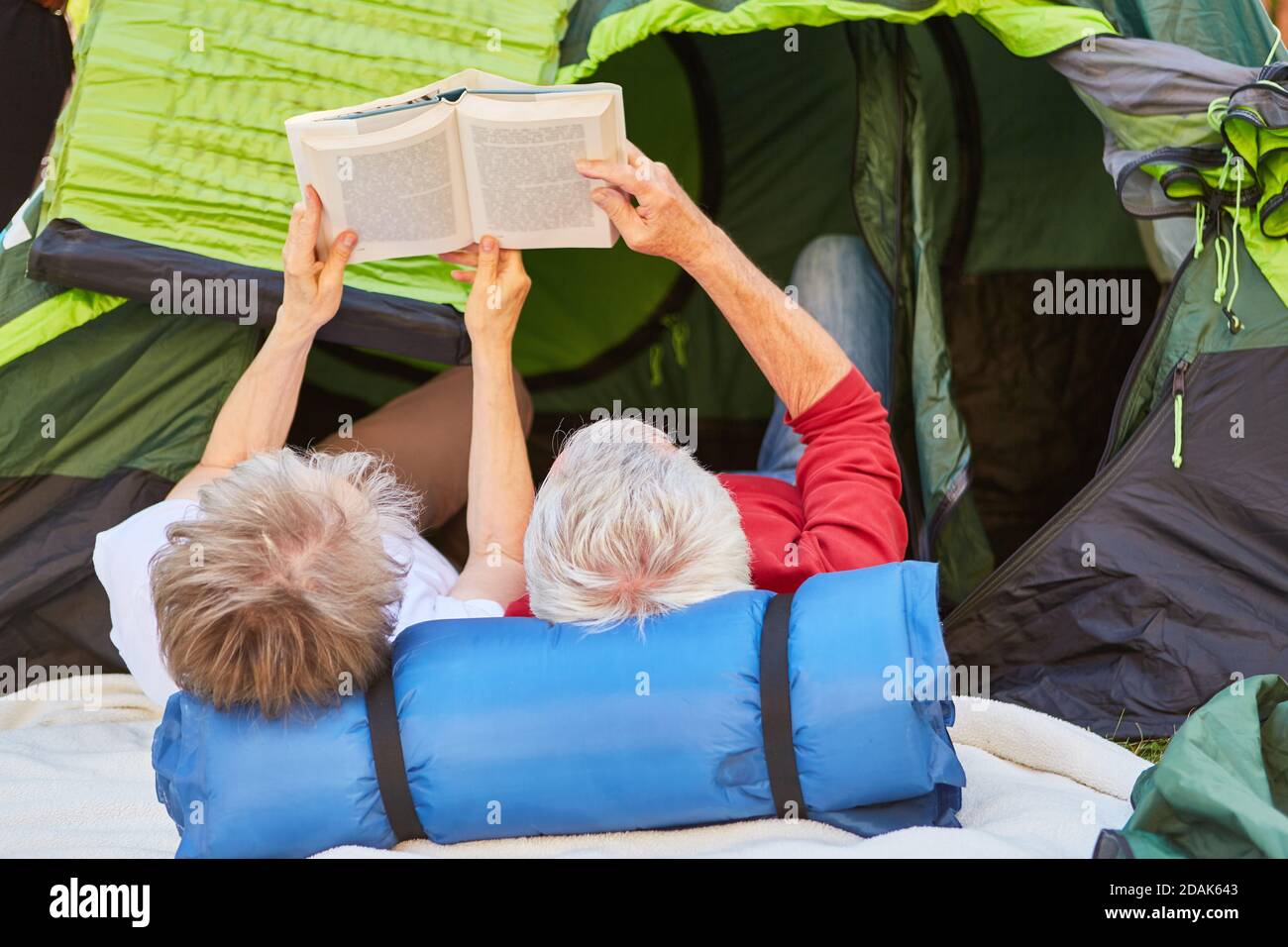 Happy senior couple reading a book together in front of the tent on ...
