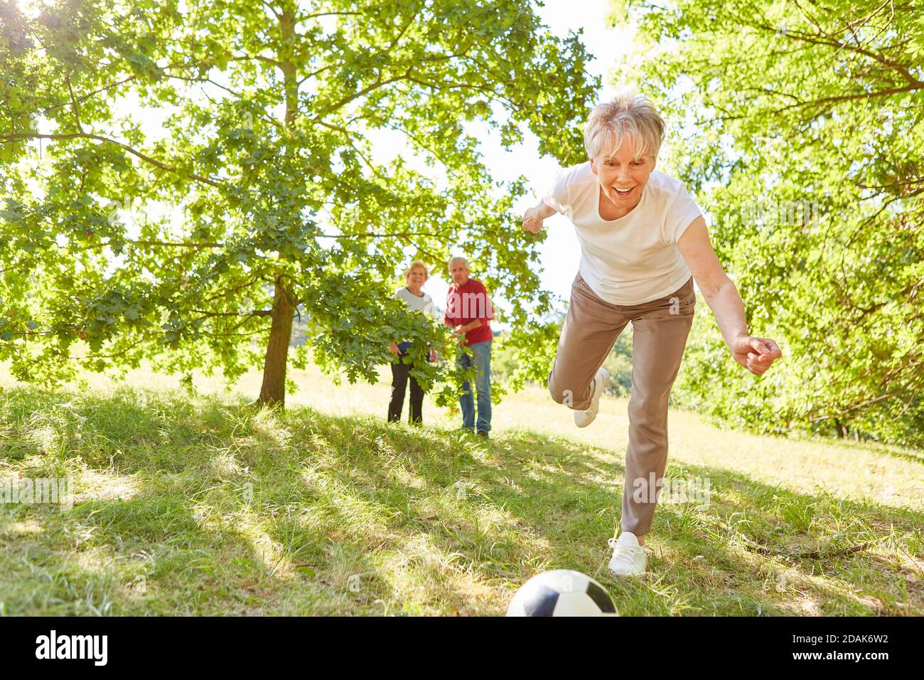 Vital senior woman playing football in the park in summer for fitness ...
