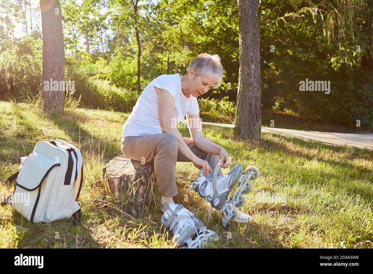Senior woman putting on inline skates in the summer in nature before ...