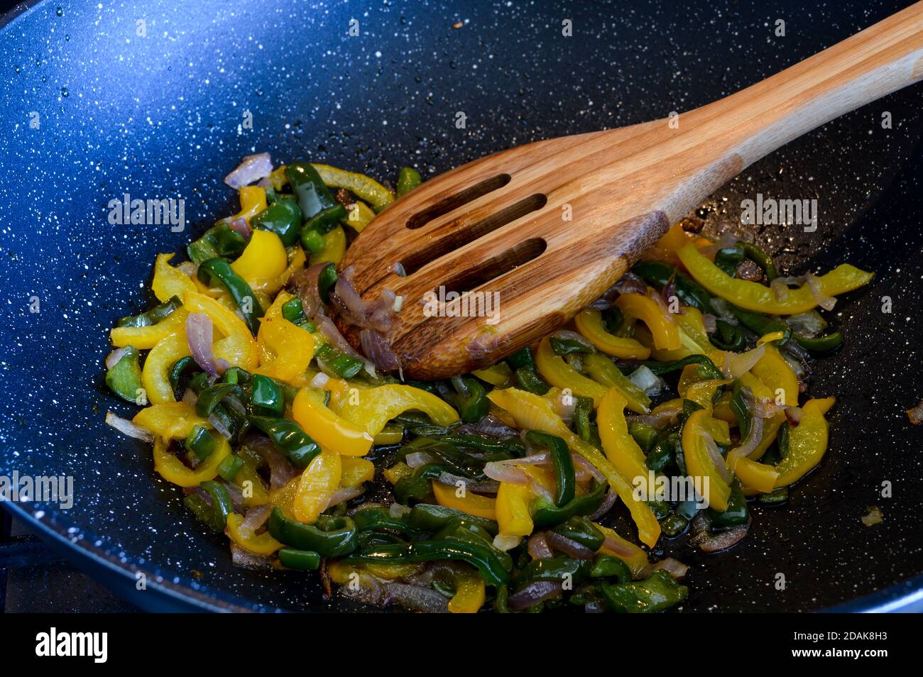 Cooking sliced green and yellow peppers with onions on a frying pan ...