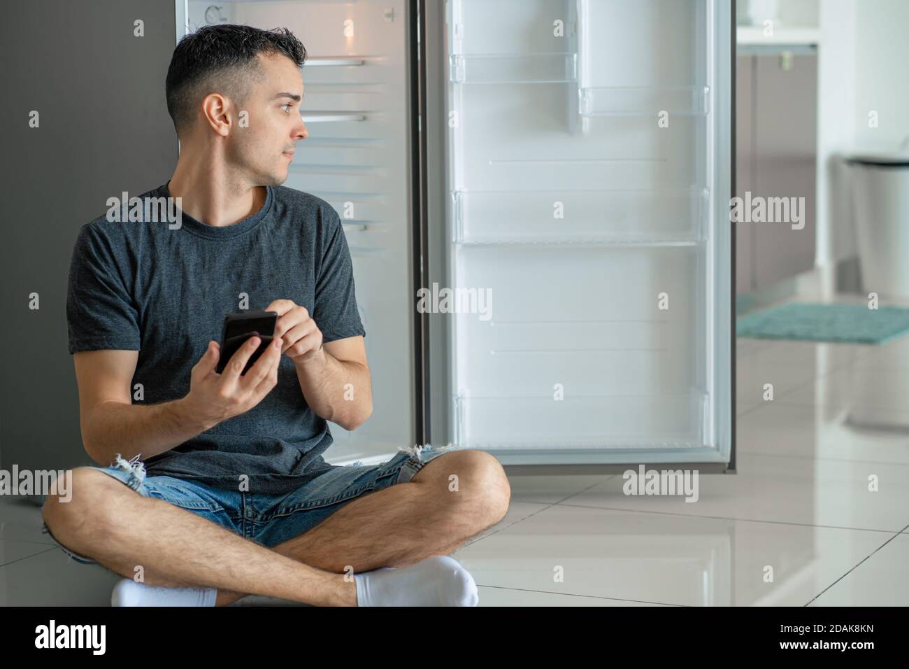 A young guy orders food using a smartphone. Empty refrigerator with no ...