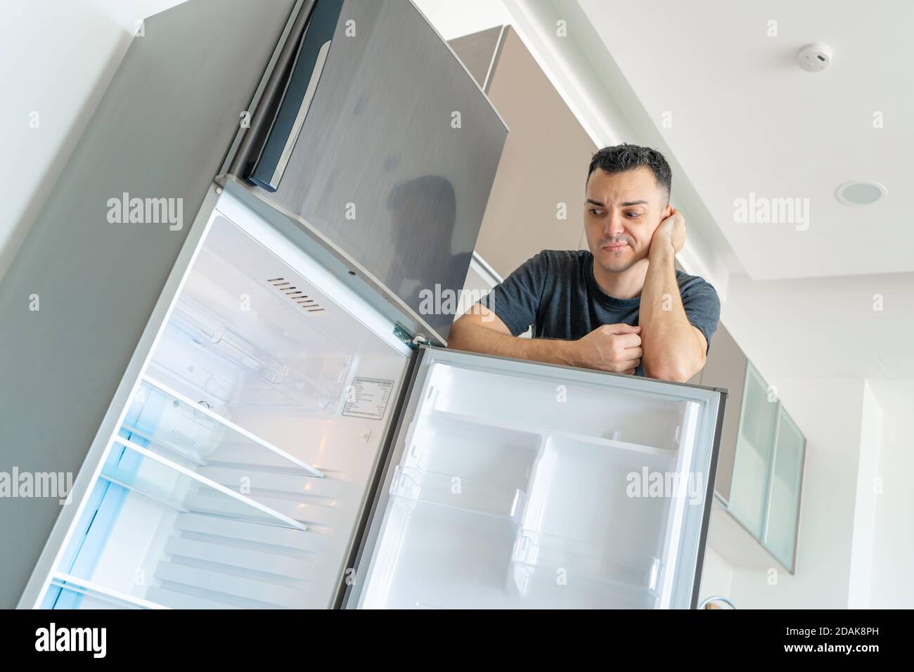 The guy is sad near the empty refrigerator without food. Food delivery ...