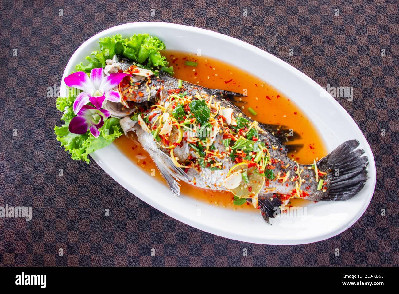 Steamed sea bass fish with lemon put a white ceramic dish on leather ...