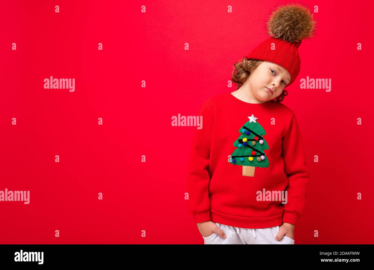 cool blond kid in warm hat and sweater with christmas tree on red ...