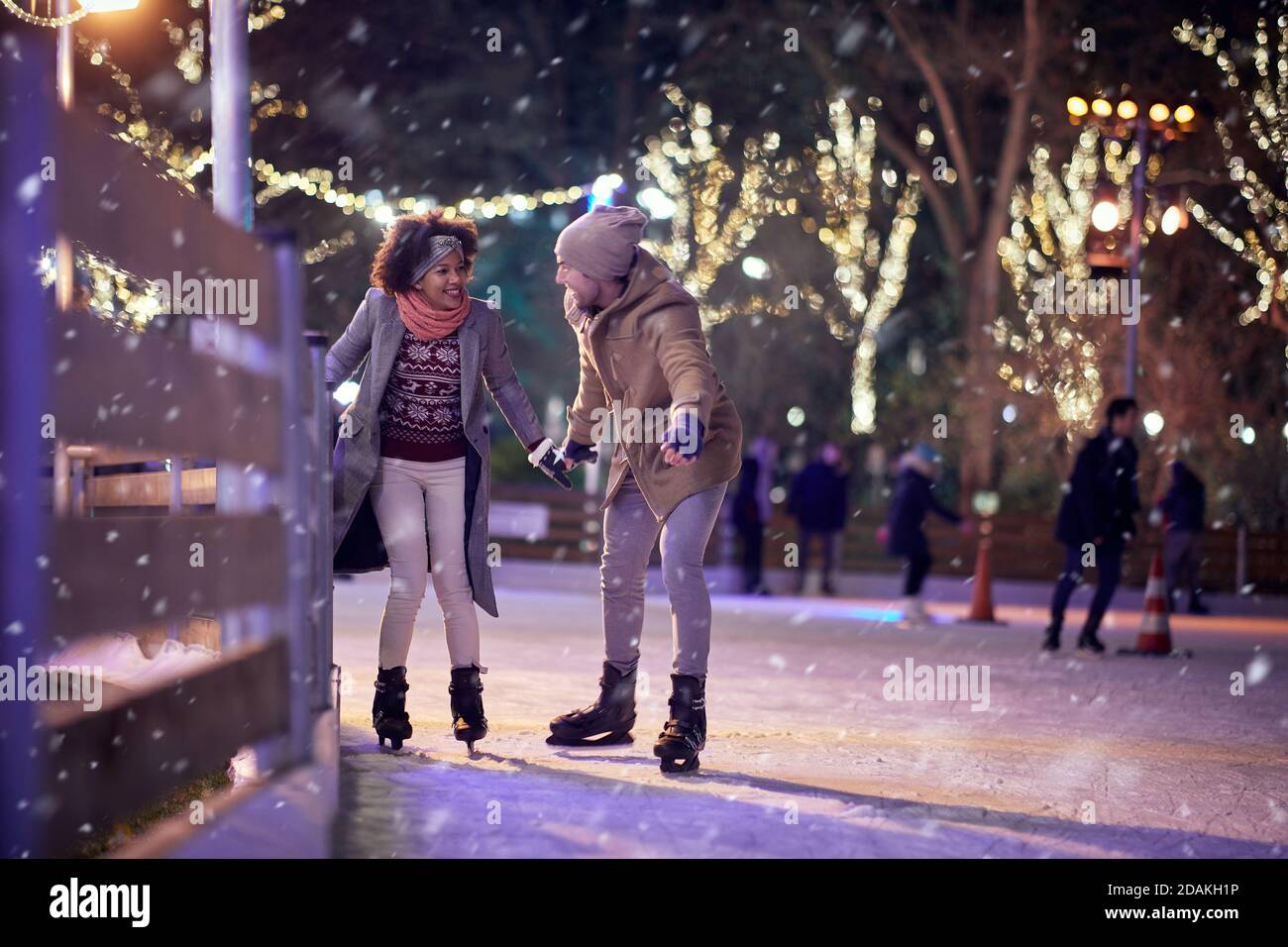 A young couple enjoying learning to skate at ice rink on a beautiful ...