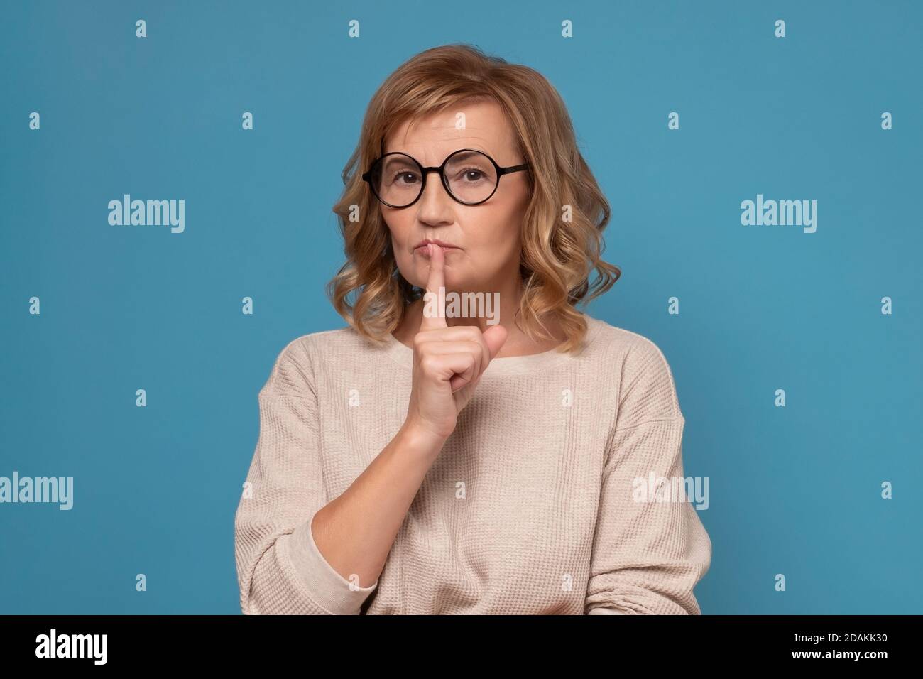 Shh, Keep silence concept. Serious woman in glasses gesturing hush sign ...