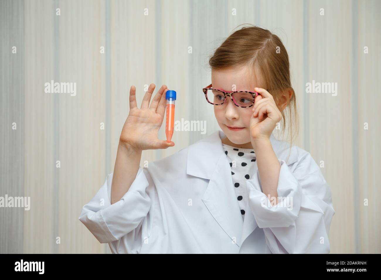 Little girl in a doctor s smock examines test tubes with tests ...