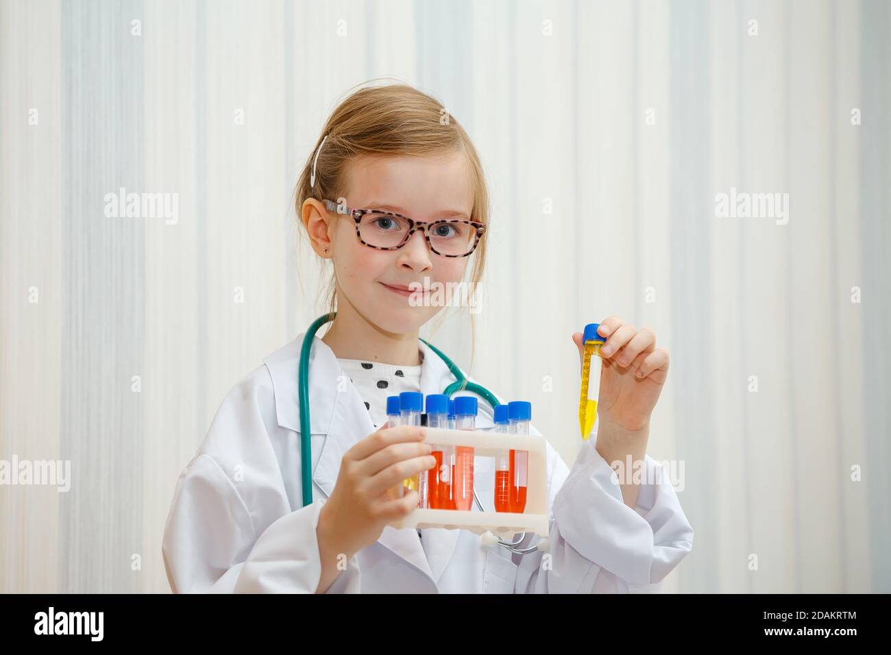 Little girl in a doctor s smock examines test tubes with tests ...