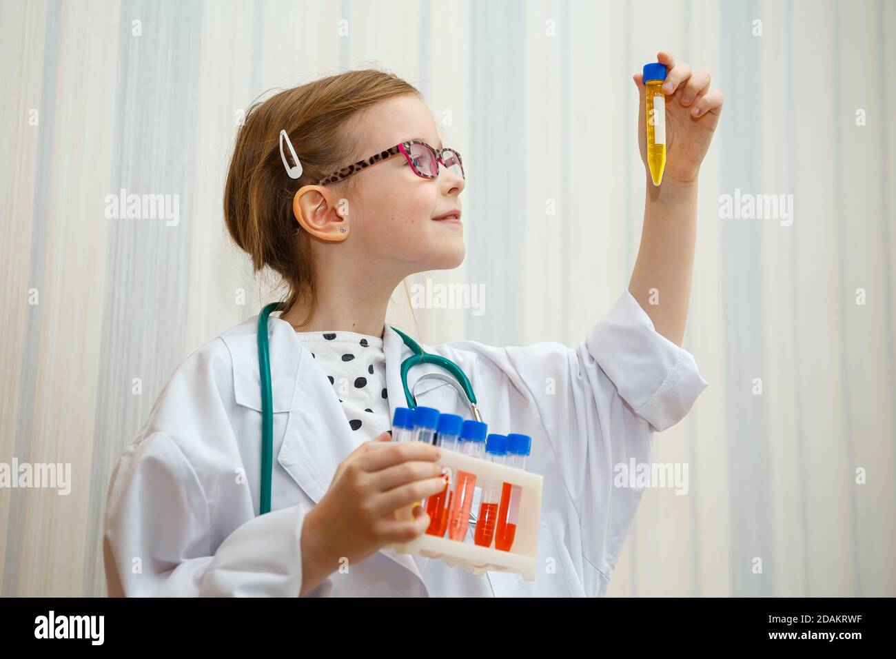 Little girl in a doctor s smock examines test tubes with tests ...
