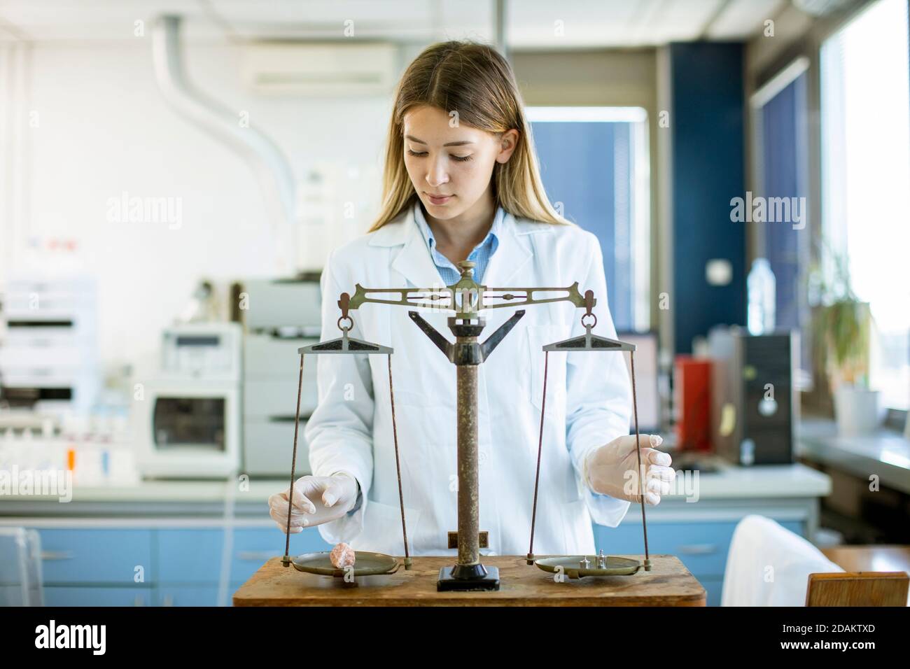 Pretty young female researcher measuring weight of the mineral sample ...