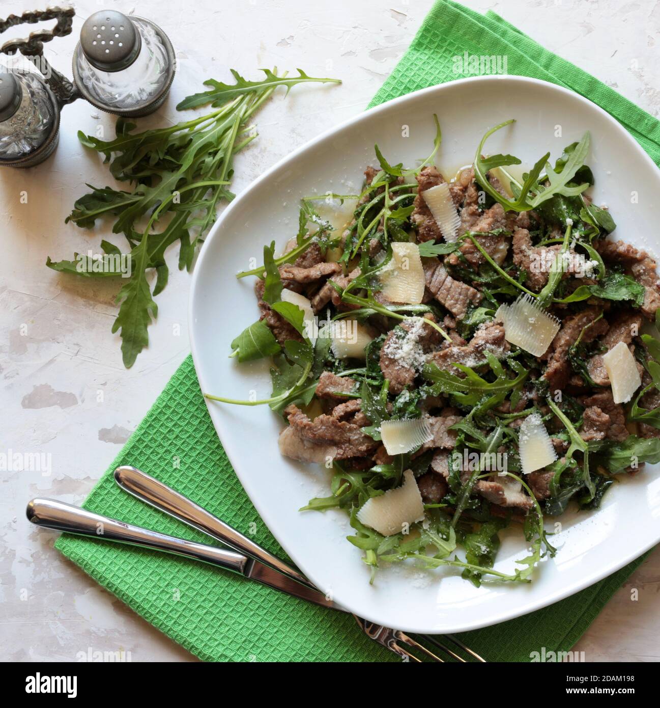 Streaks of meat with rocket and parmesan on a white plate. Top view ...