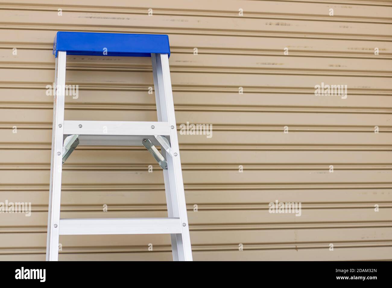 An aluminum foldable ladder leaning on the metal wall Stock Photo - Alamy