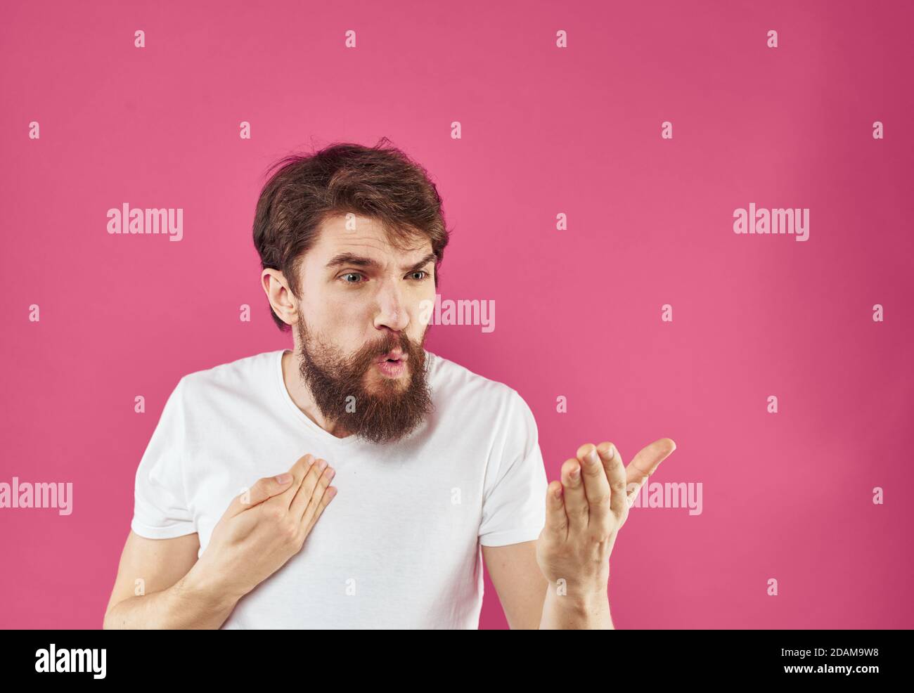 An indignant man gestures with his hands in a white T-shirt on a pink ...