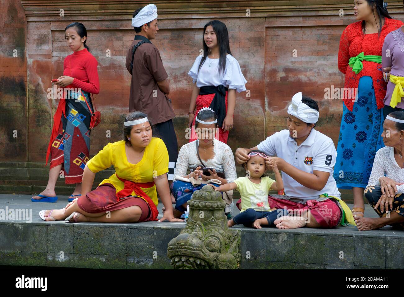 Balinese family in traditional Bainese attire sitting around a pool at ...