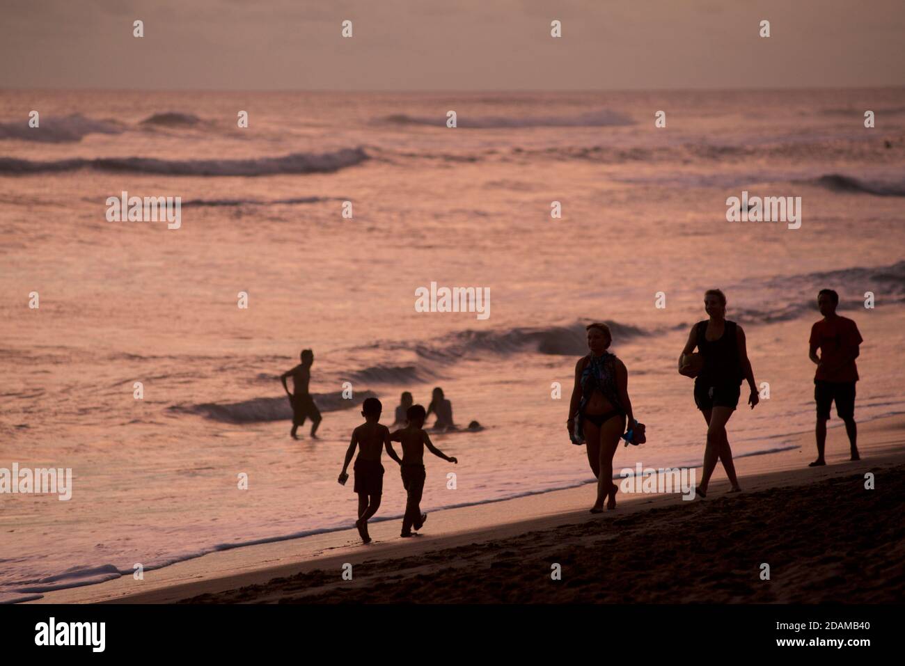 Beachgoers silhouetted against the sea, Nelayan Beach at sunset, North ...