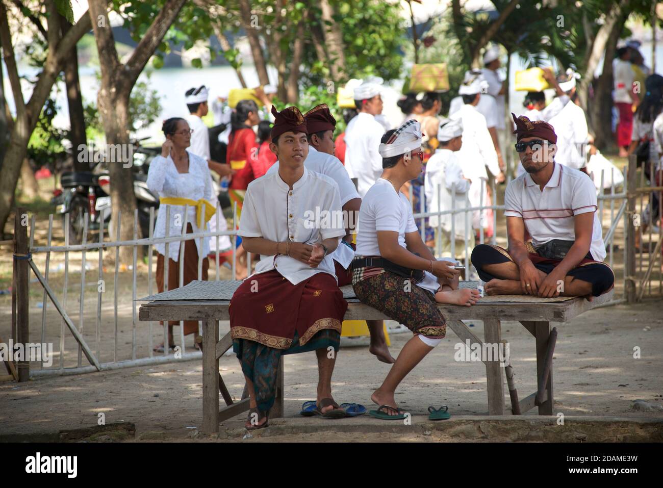 Balinese men in traditional festive attire relaxing at Sakenan temple ...