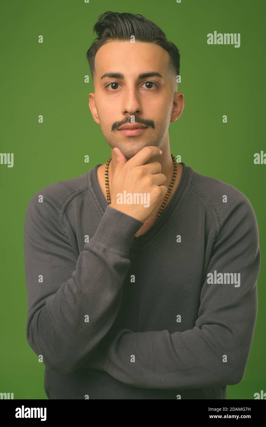 Young handsome Iranian man with mustache against green background Stock ...