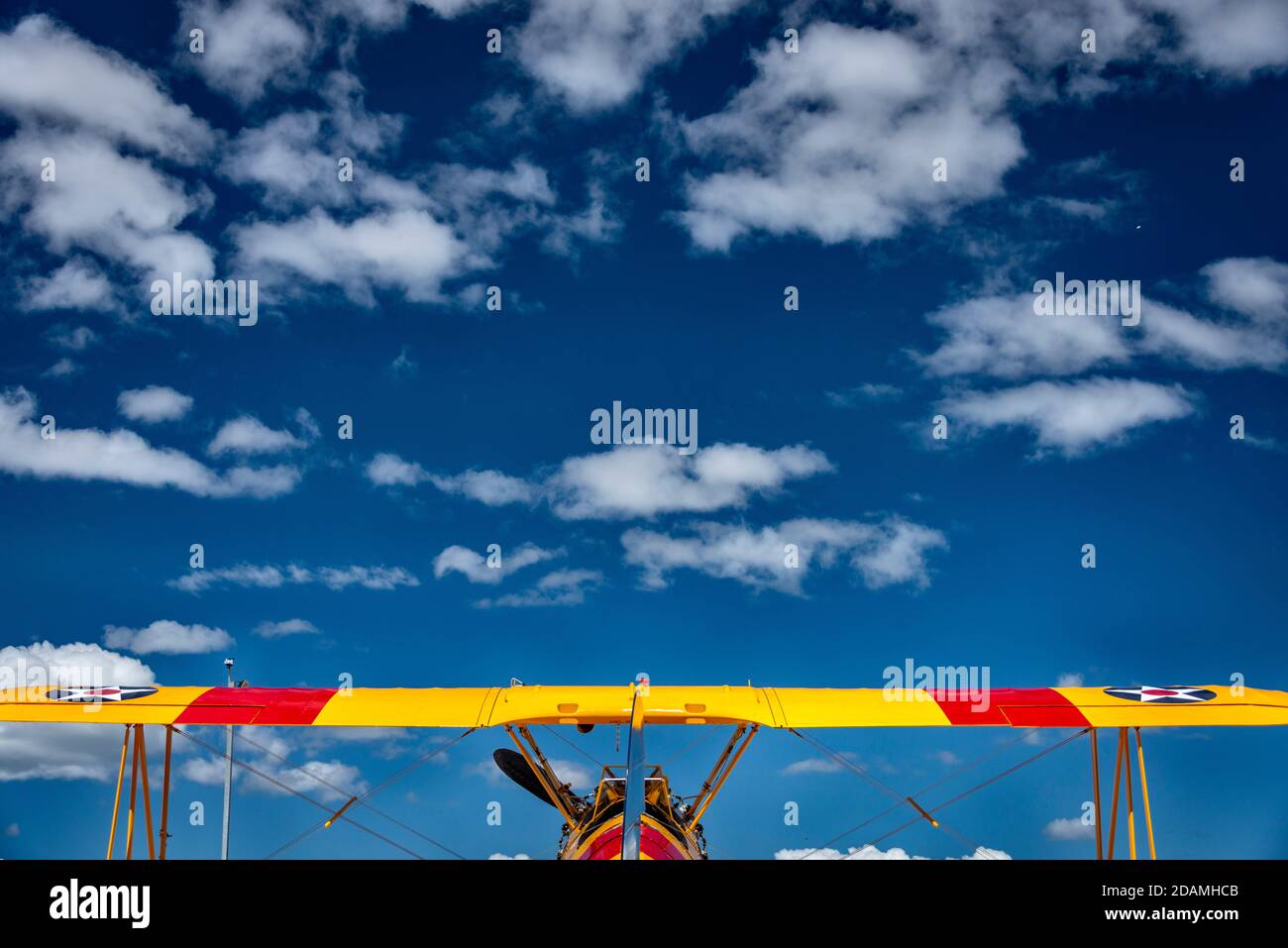 the top wing of a red and yellow biplane against a vast blue sky with ...