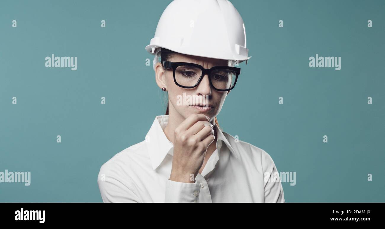 Pensive young businesswoman wearing a safety helmet and thinking with ...