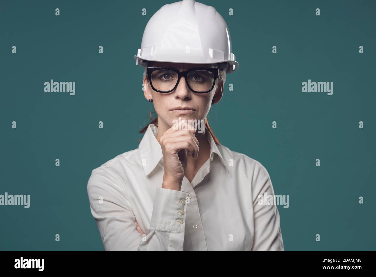 Pensive young businesswoman wearing a safety helmet and thinking with ...