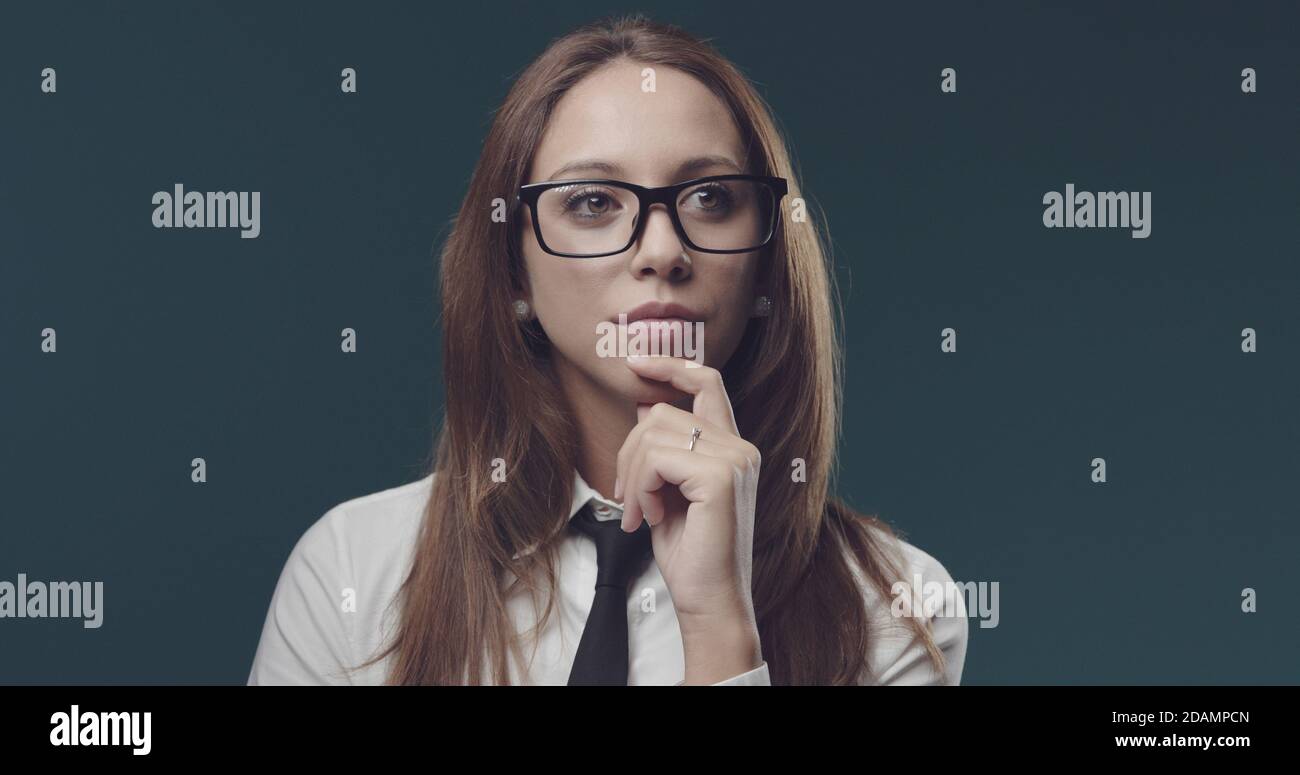 Pensive young businesswoman thinking with hand on chin, she is wearing ...