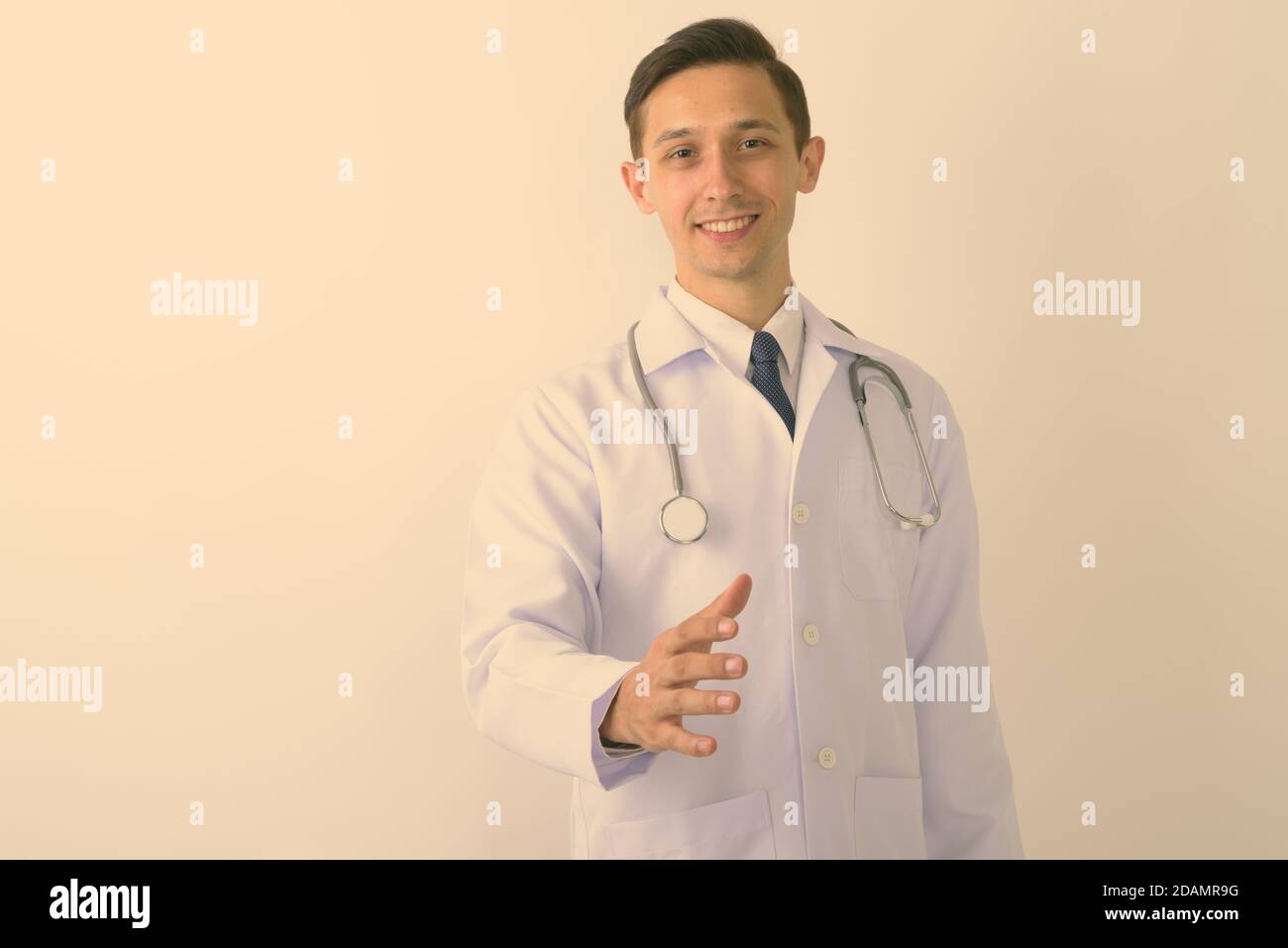 Studio shot of young happy man doctor smiling while giving handshake ...