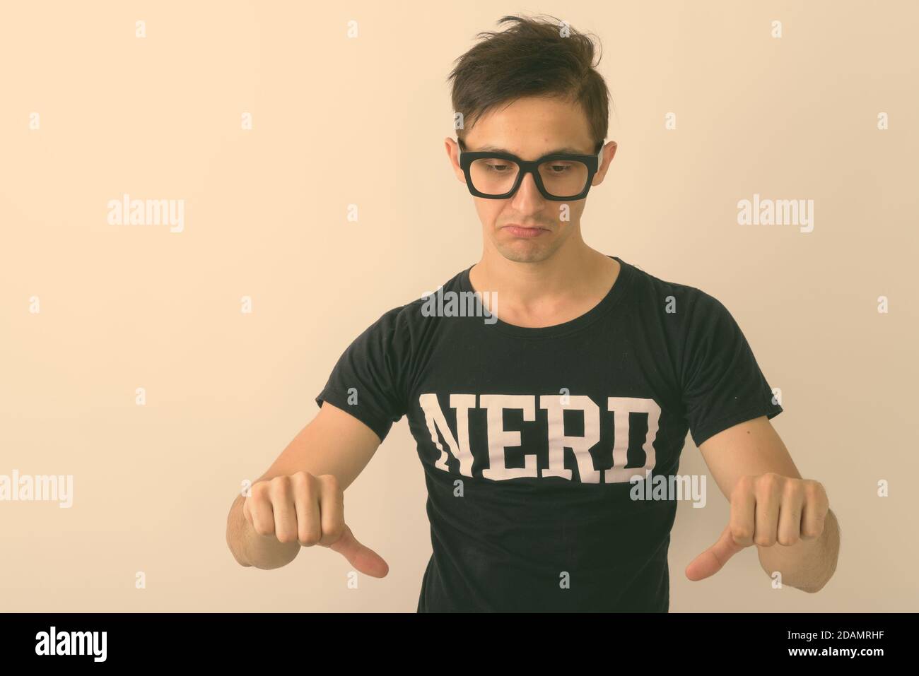 Studio shot of young nerd man looking sad and giving thumbs down while ...