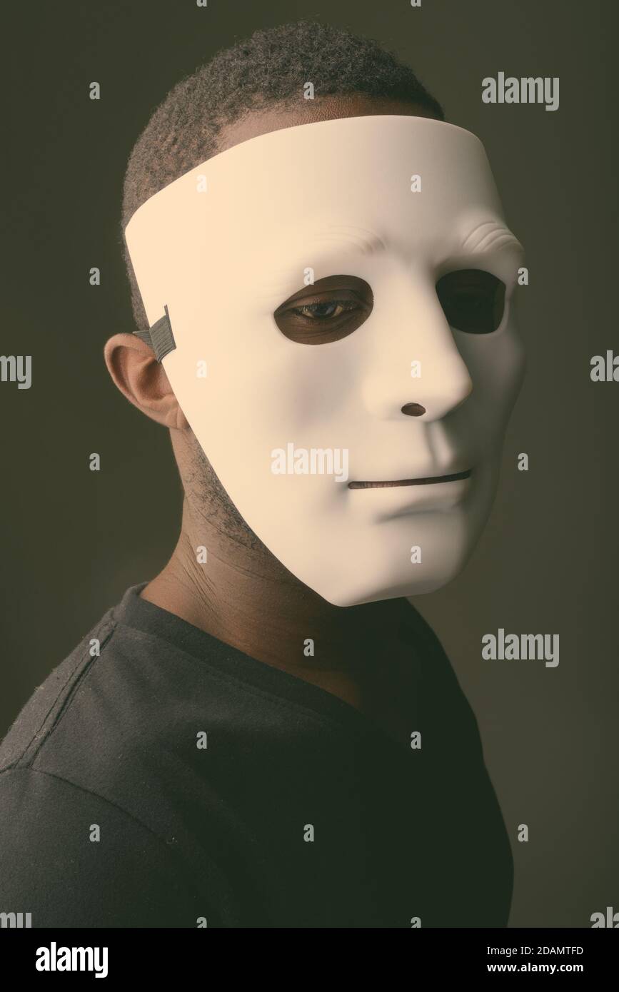 Studio shot of young black African man in dark room wearing mask Stock ...
