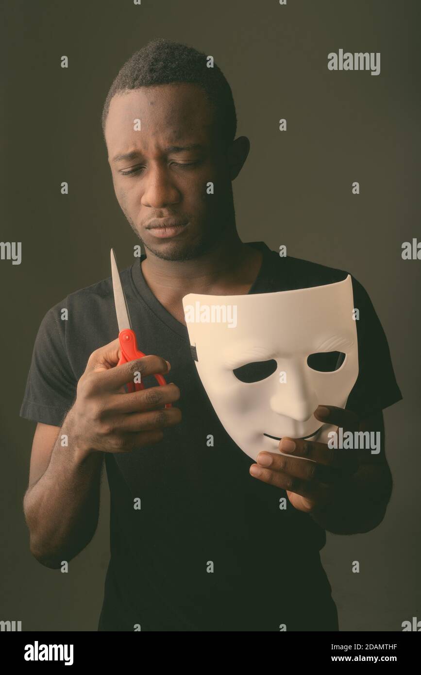 Studio shot of young black African man holding mask and scissors in ...