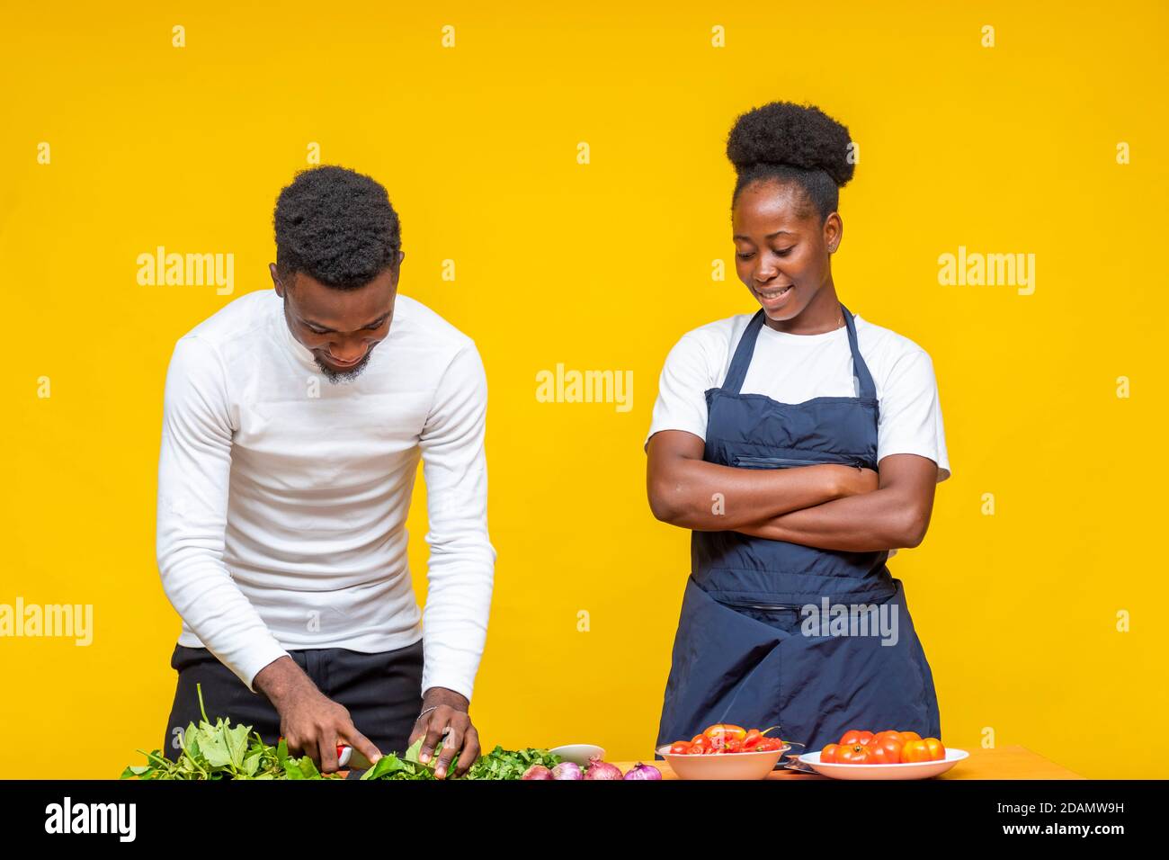 african couple cooking together, the woman watching as the man slices ...