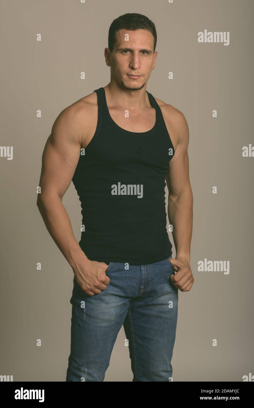 Studio shot of young muscular Persian man standing against gray ...