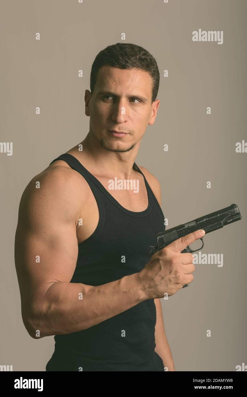 Studio shot of young muscular Persian man thinking while holding gun ...