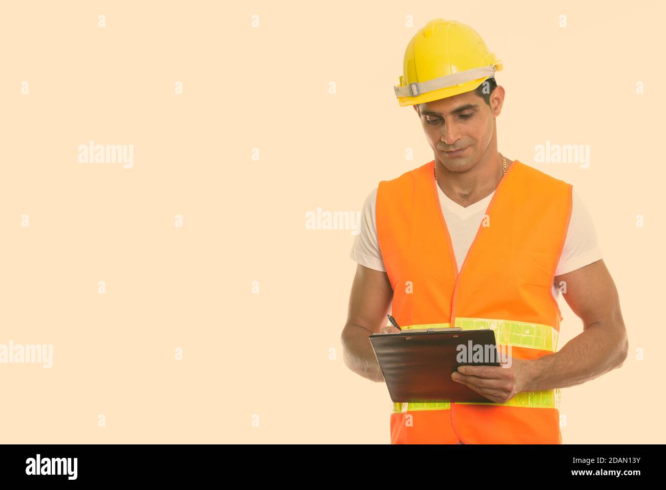 Studio shot of young muscular Persian man construction worker writing ...