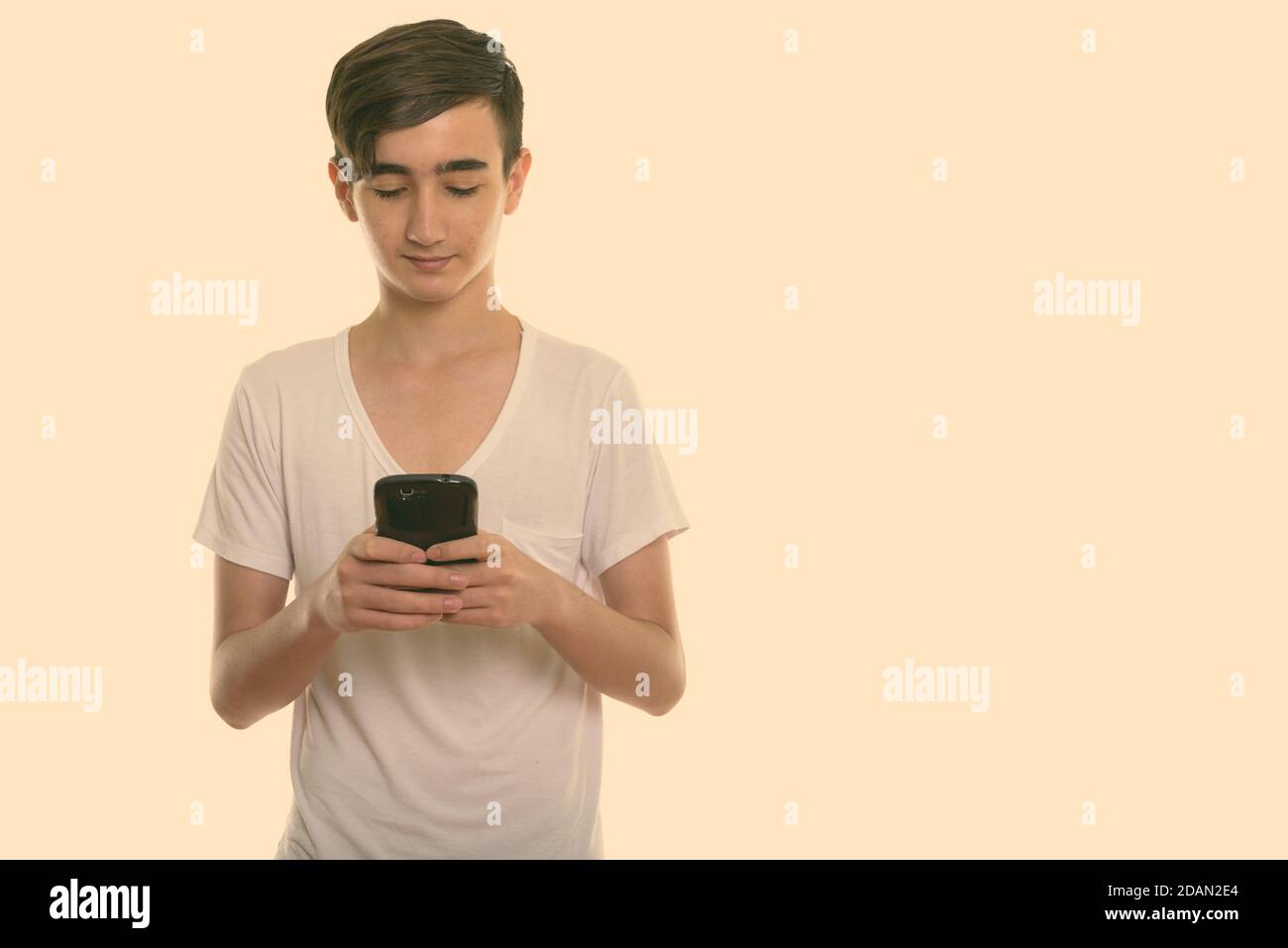 Studio shot of young handsome Persian teenage boy using mobile phone ...
