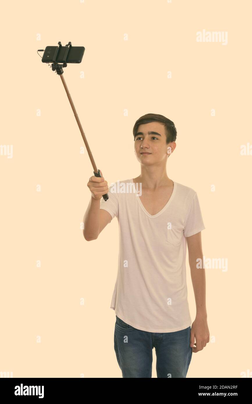 Studio shot of young handsome Persian teenage boy holding selfie stick ...