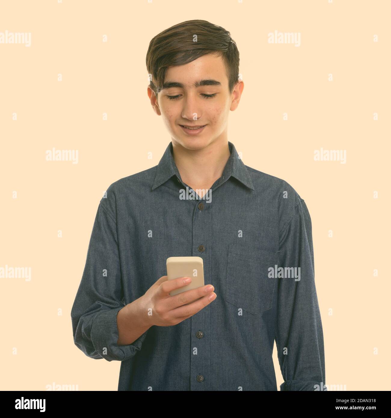 Studio shot of young happy Persian teenage boy smiling while using ...