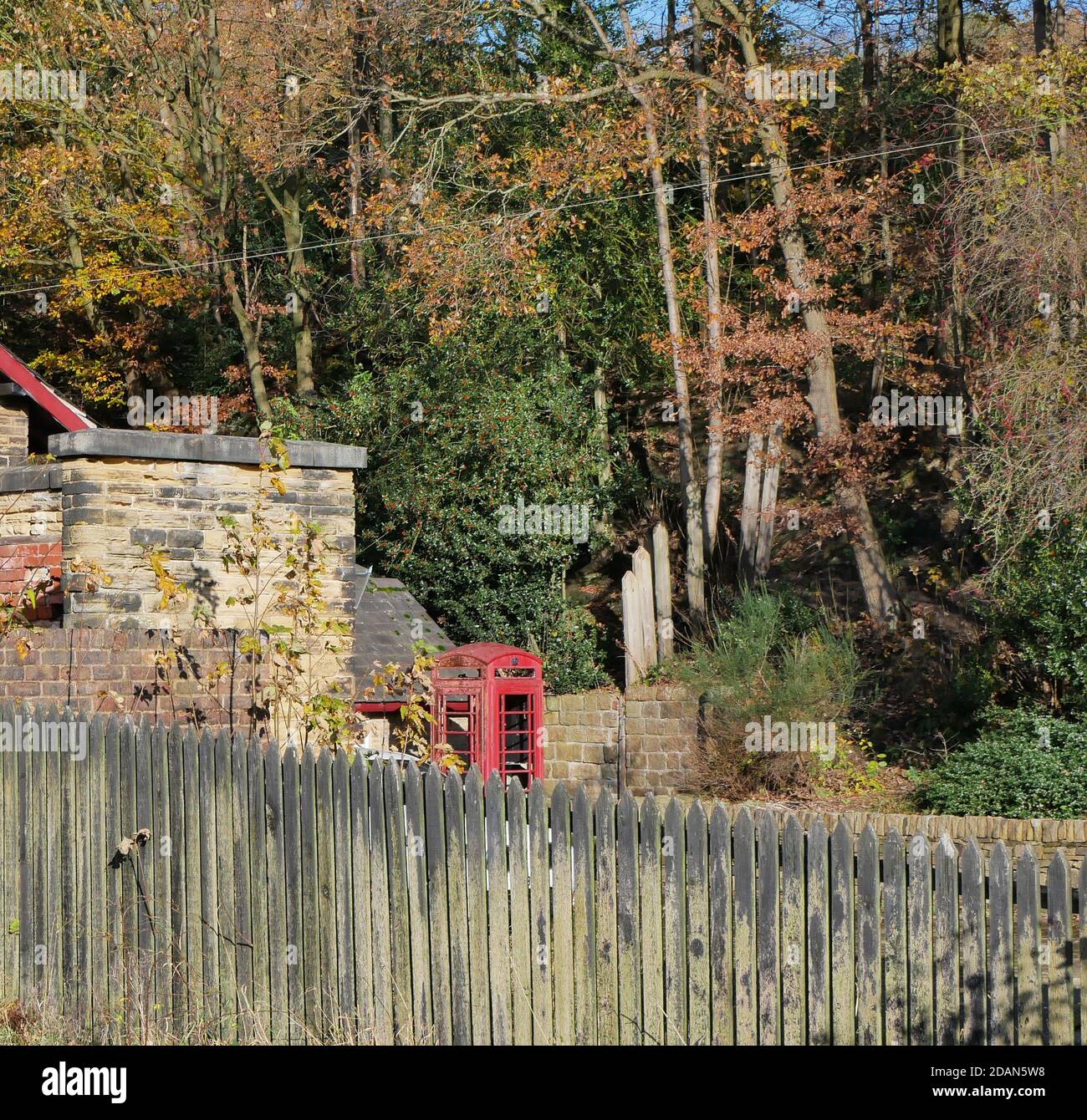 Old rusty red British telephone box stood in garden behind a wood fence ...