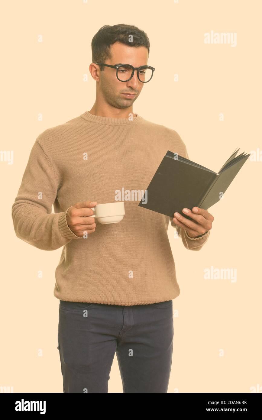 Young handsome Iranian man reading book while holding coffee cup Stock ...