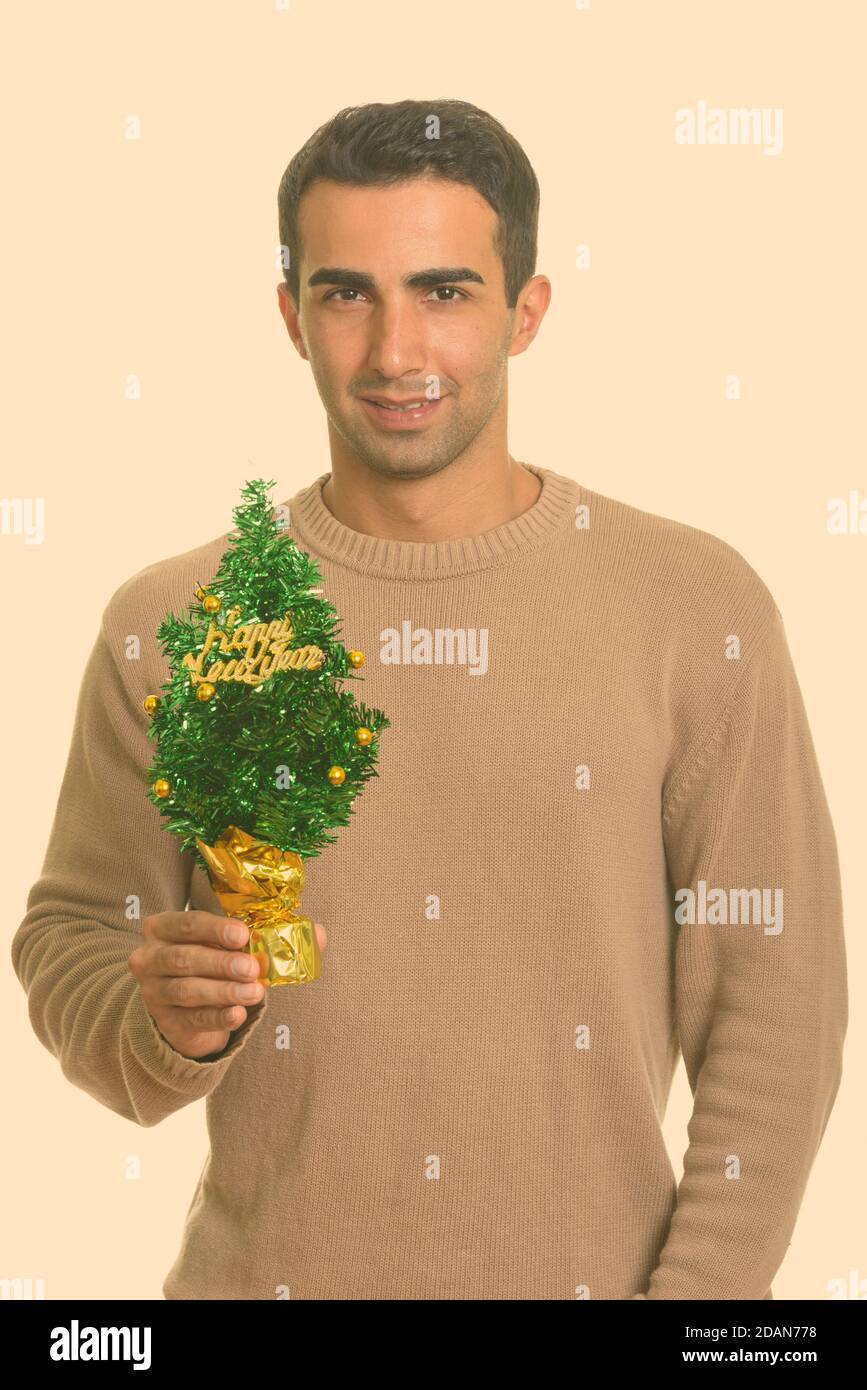 Young happy Iranian man holding Merry Christmas tree ready for ...
