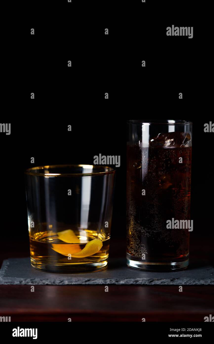 Whiskey with lemon zest and cola with clear ice served on slate plate ...