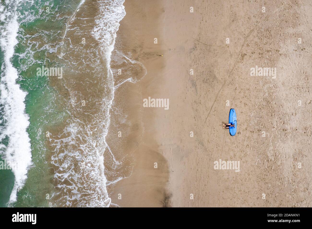 Surfer sitting on surf board on a beach from above Stock Photo - Alamy