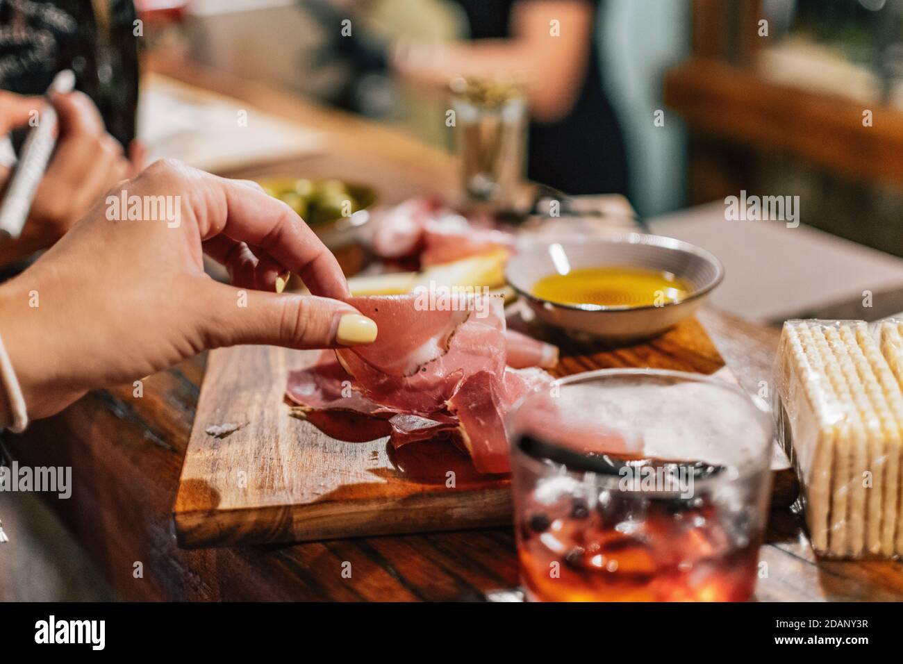 Female hand taking a piece of cured pork meat from a charcuterie board ...