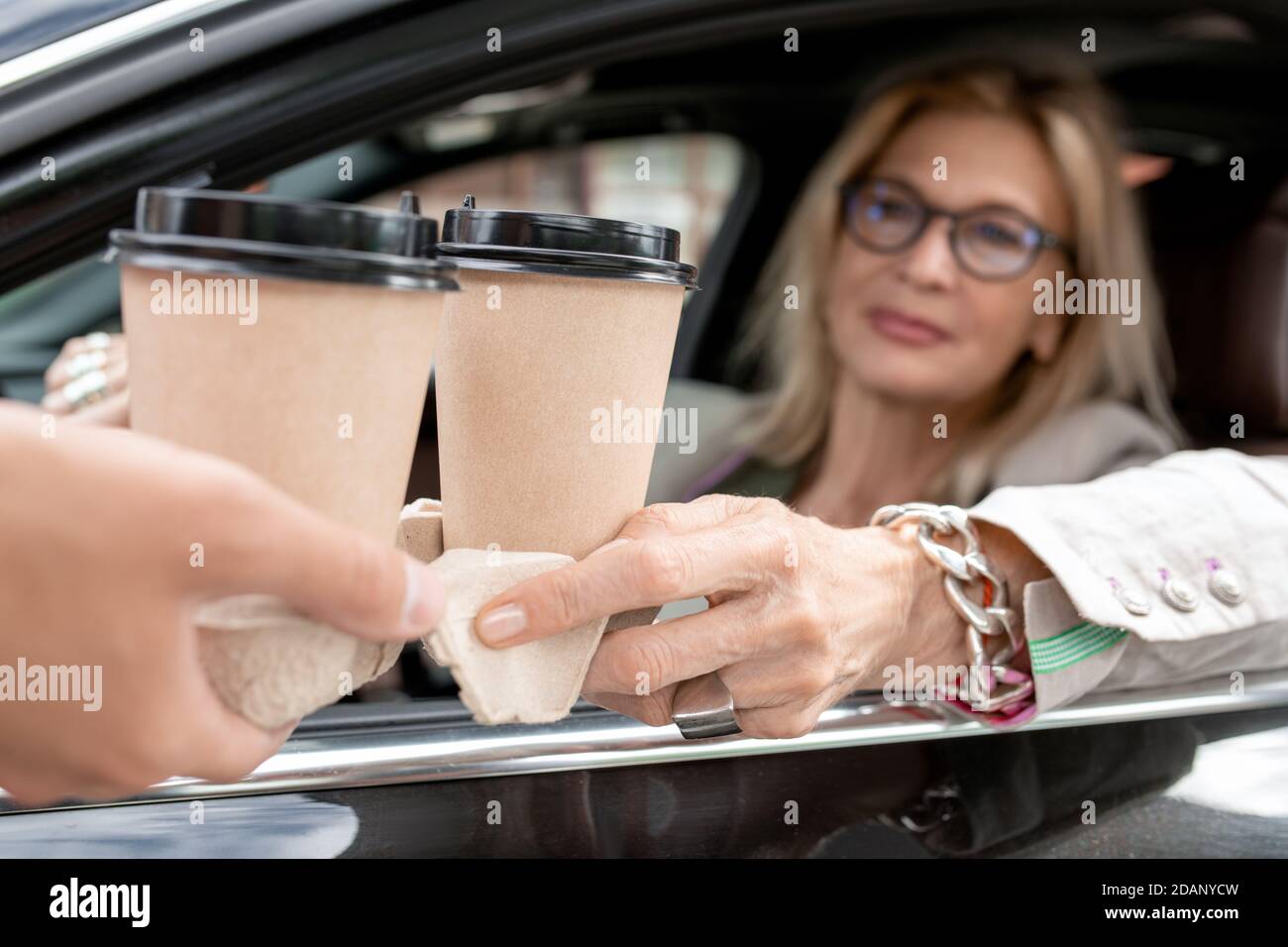 Hand of mature female taking two paper glasses of coffee through car ...