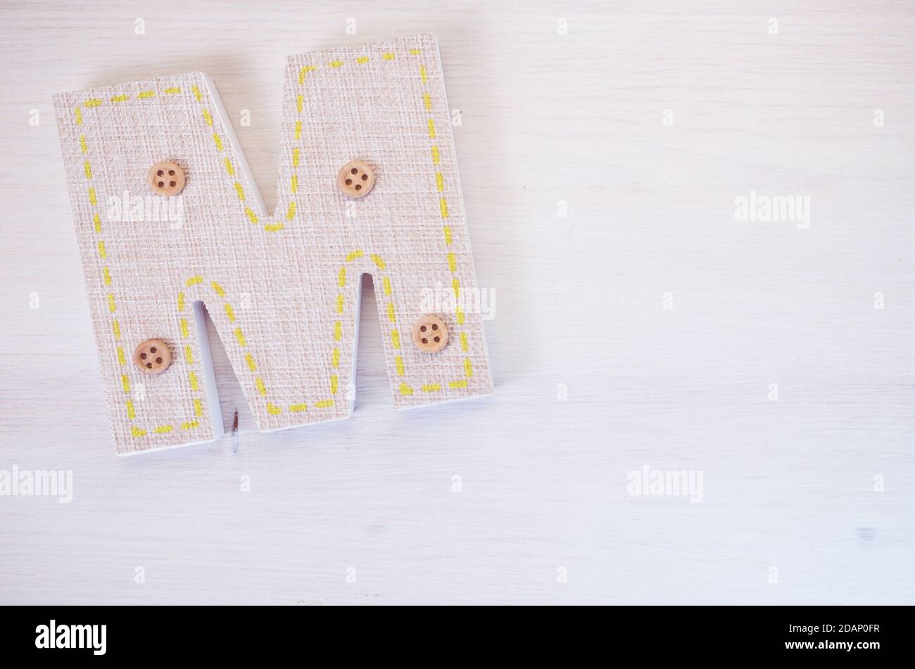Overhead shot of a handcrafted letter M with buttons on wooden surface ...